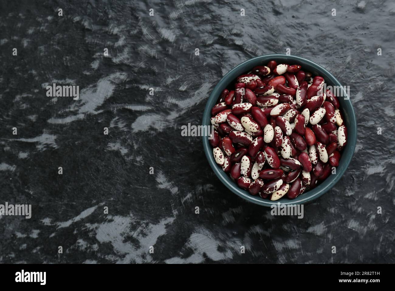 Bowl with dry kidney beans on black textured table, top view. Space for ...
