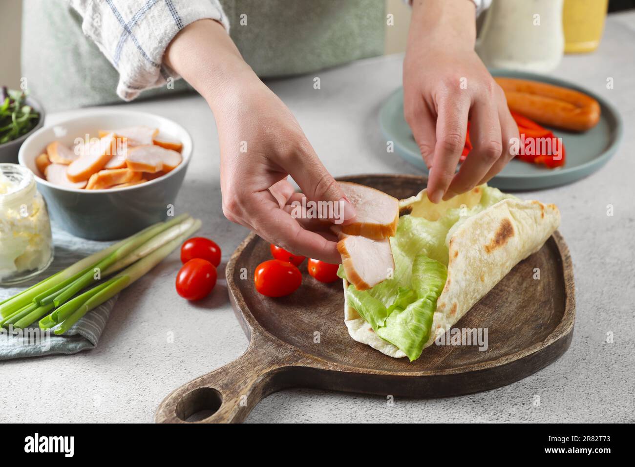 Woman cooking delicious pita wrap with chicken and lettuce at light ...