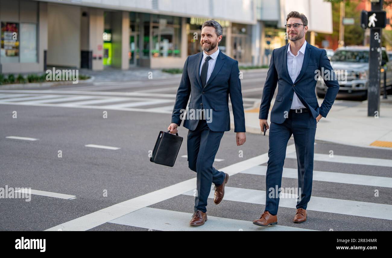 Photo of businessmen in suits walking outdoor through city street. Two ...