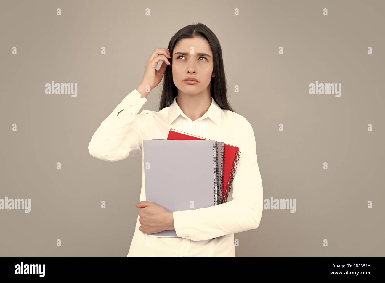Angry young woman college student holding book on isolated gray ...