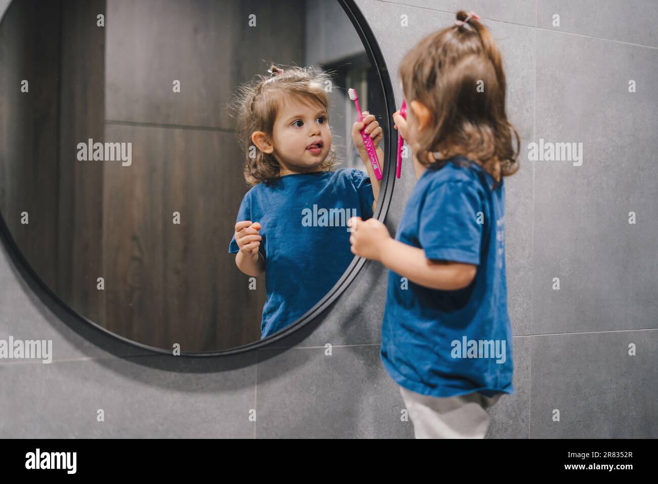 Little girl brushing her teeth early in the morning, looking in the ...