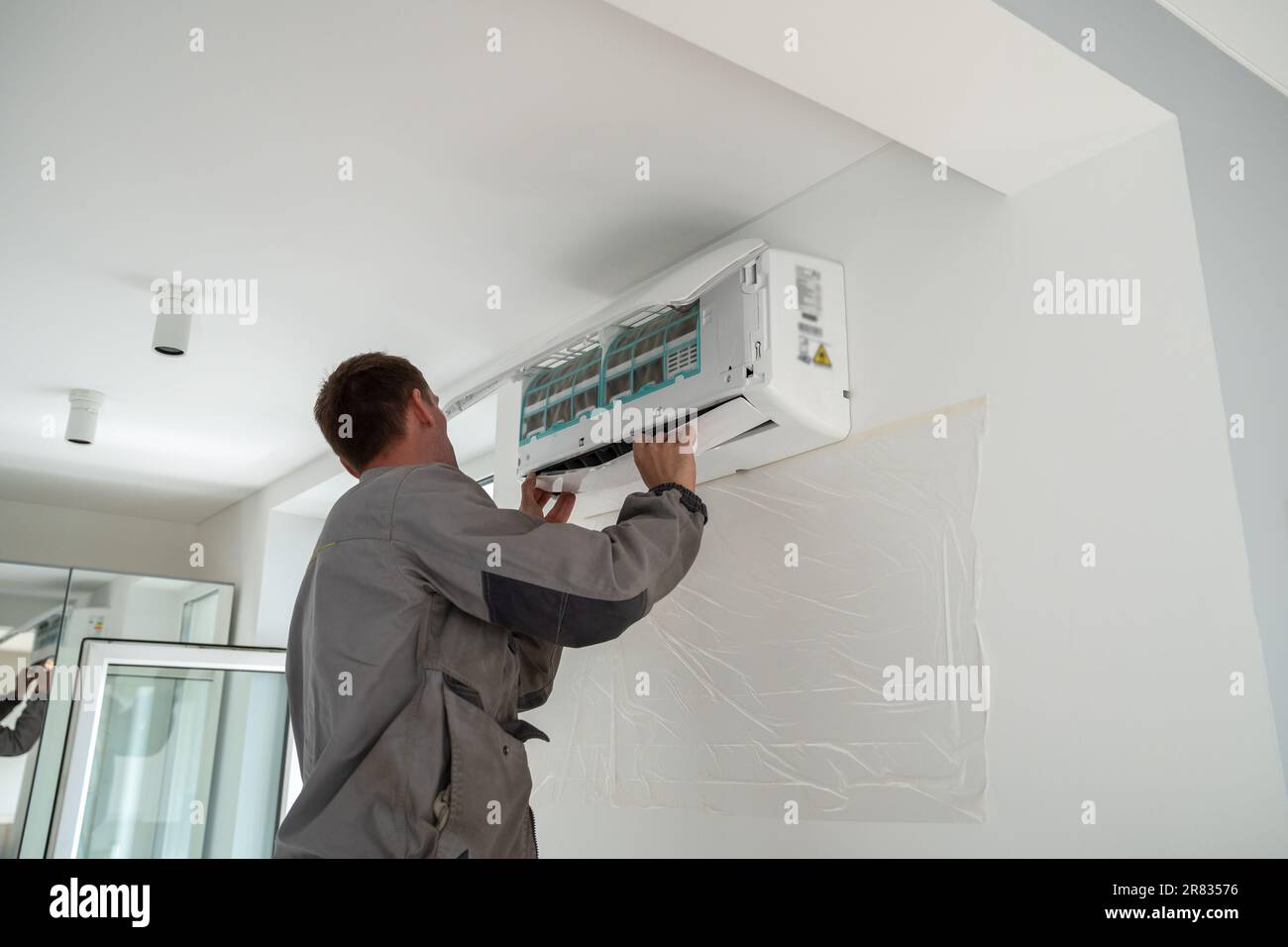 Male worker installing air conditioner in apartment during summer ...