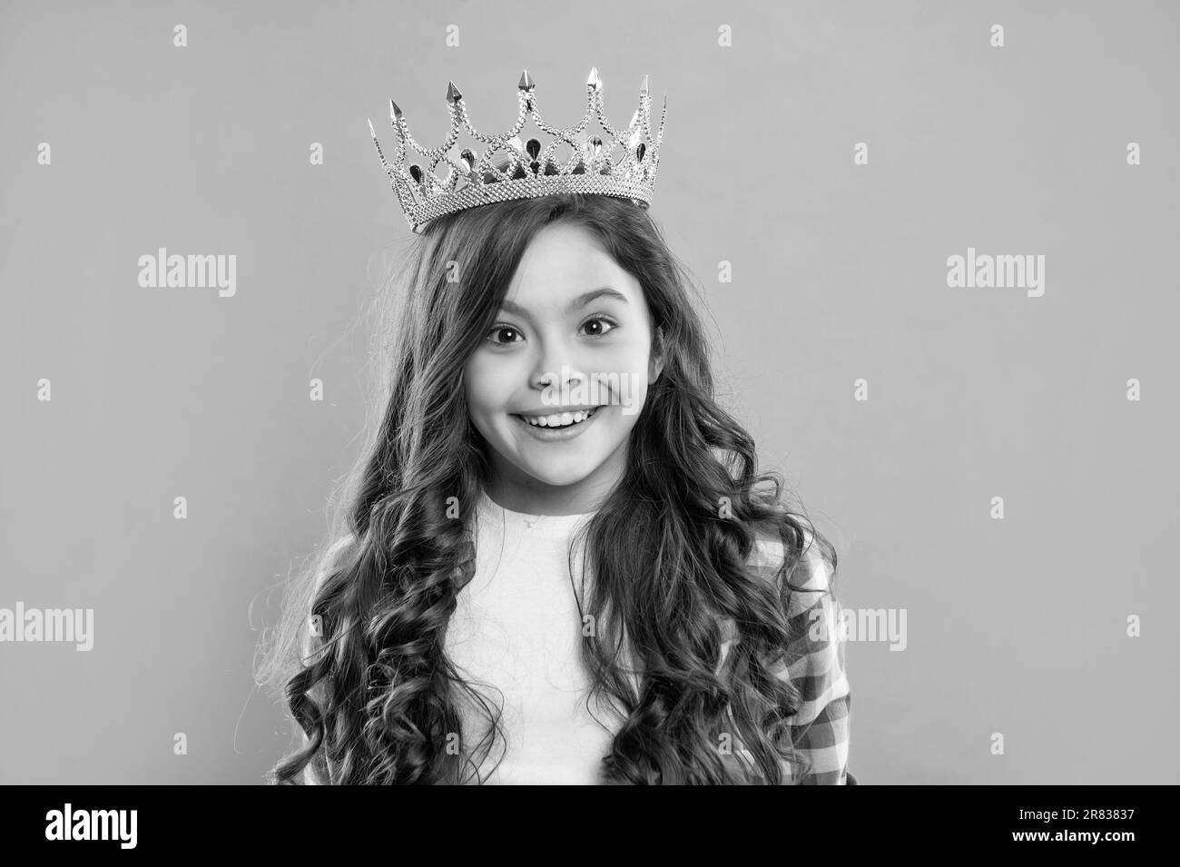 smiling child with curly hair in queen crown on blue background, smug ...