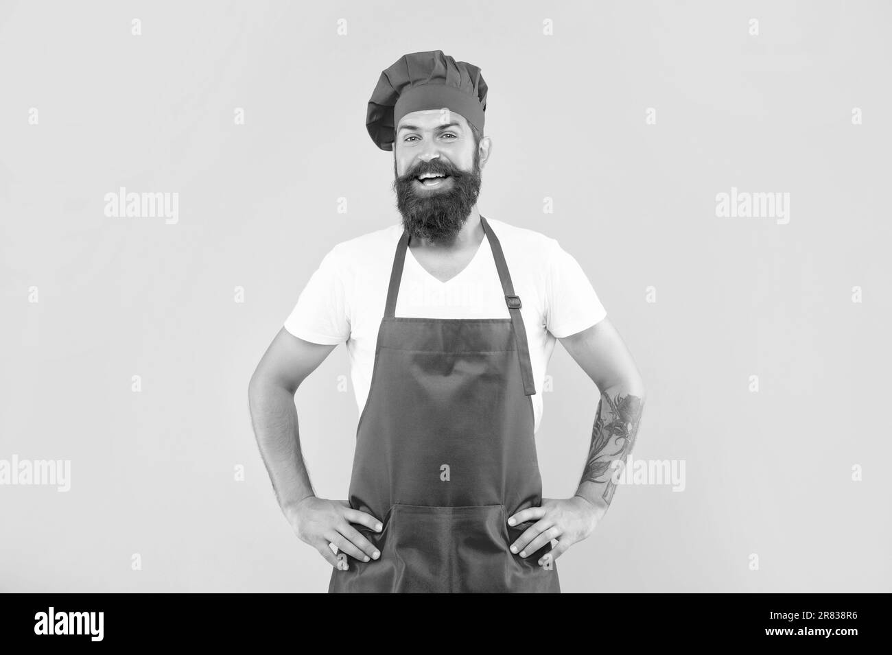Happy man in red toque and apron with arms akimbo yellow background ...