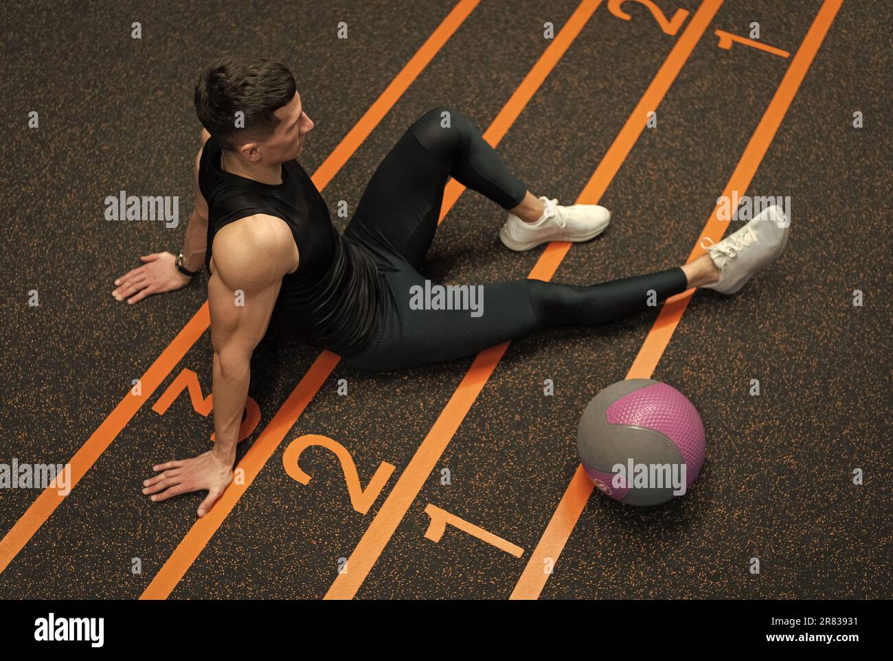 Fit man sitting on gym floor. Athlete resting after fitness ball ...
