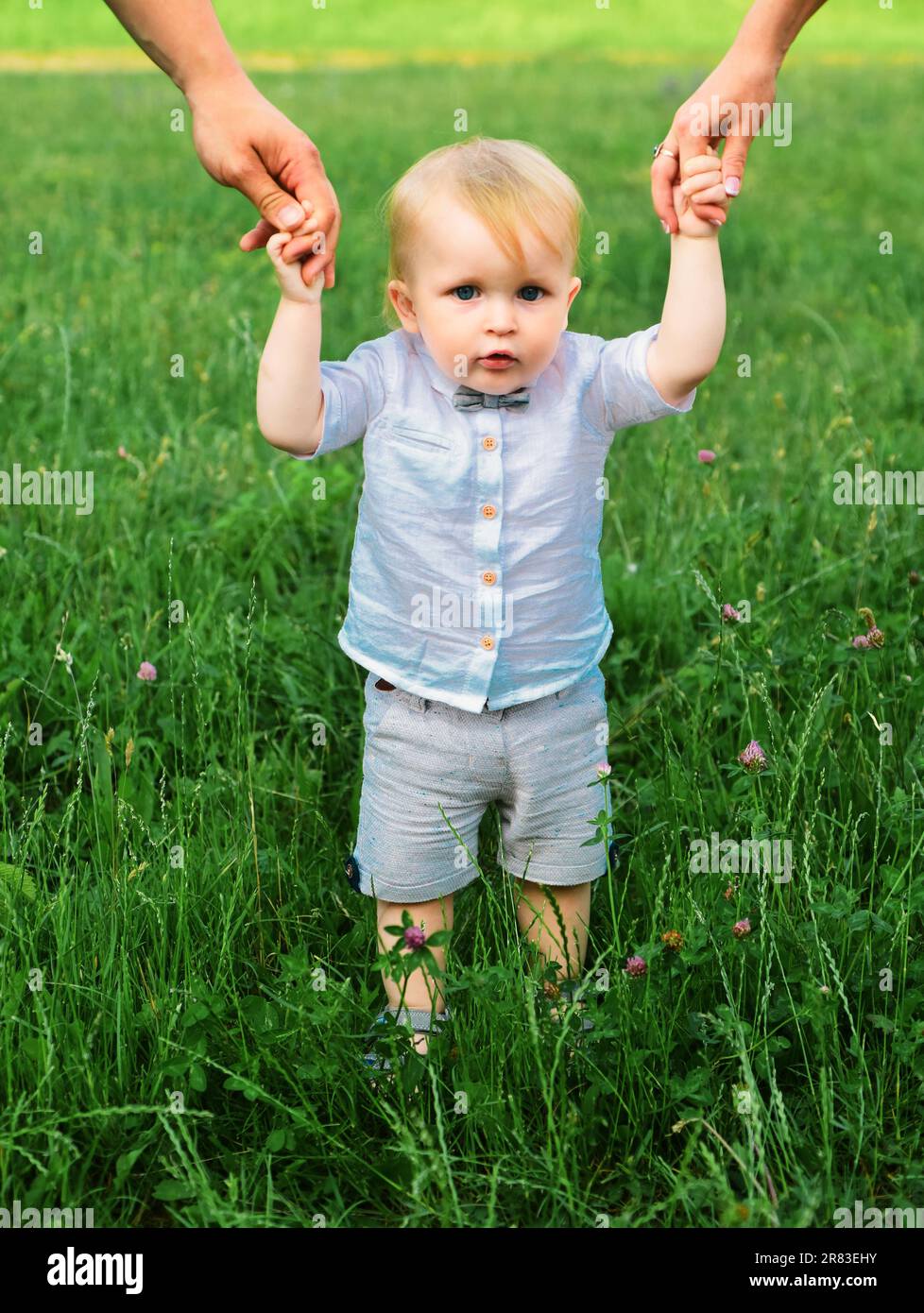 Baby child on the green grass in summer park. Parents hand and child ...
