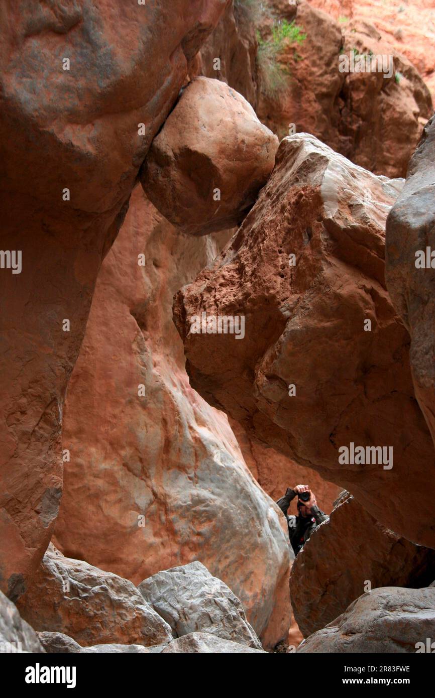 A hiker photographs a trapped boulder in a side gorge of the Dades ...