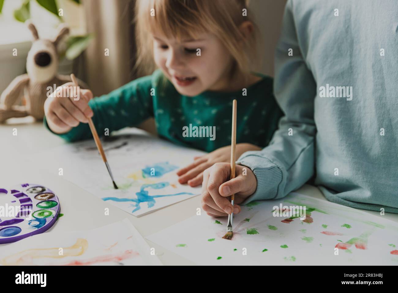 Two cute little sisters or classmates are painting on table with brush ...