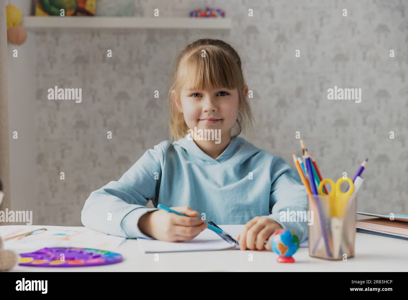 Schooler cute little girl sitting at desk in bedroom, holding a pen ...