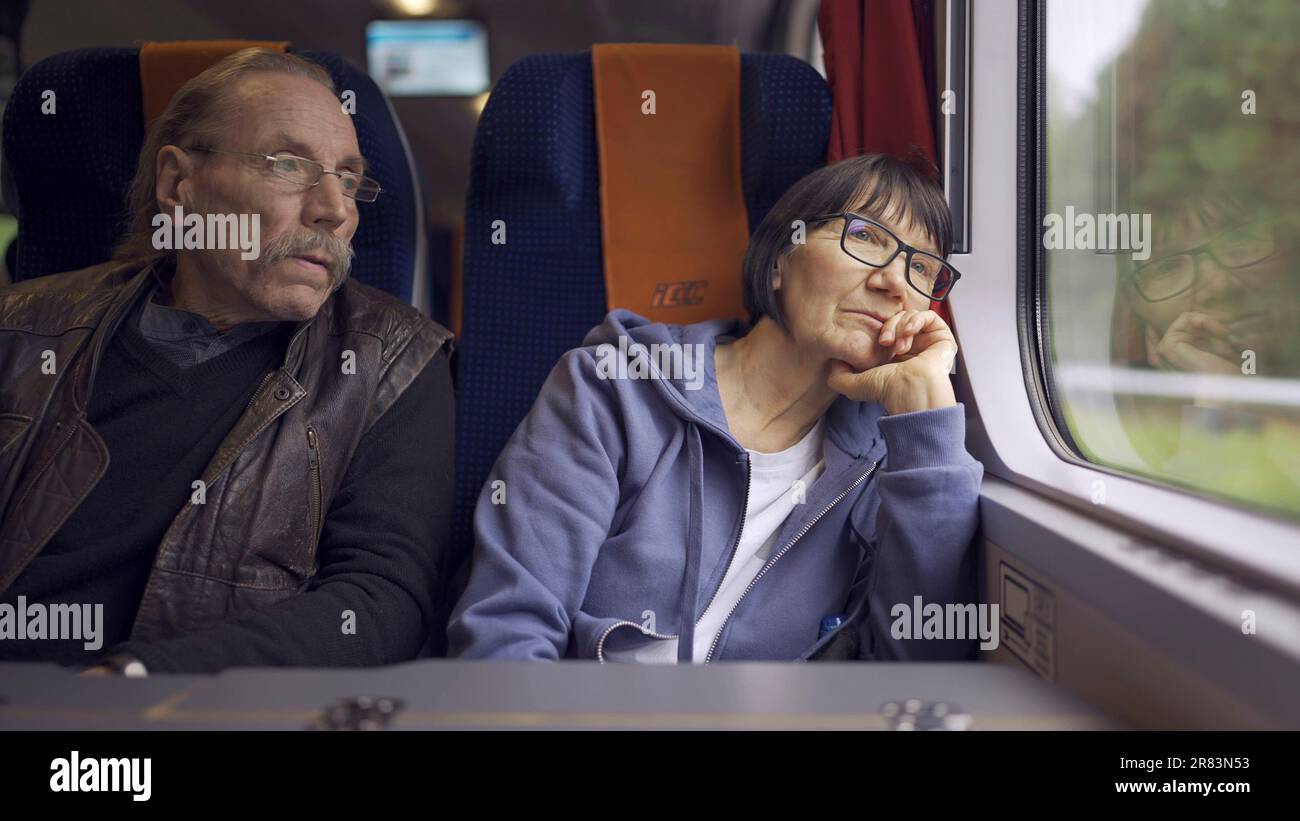 Elderly couple is riding in a train carriage and looking out the window ...