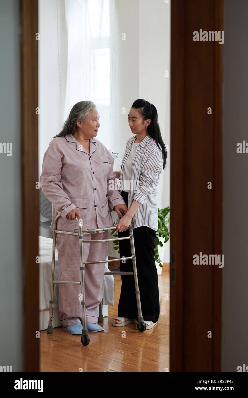Mother helping sick senior woman to walk with walker for the first time ...