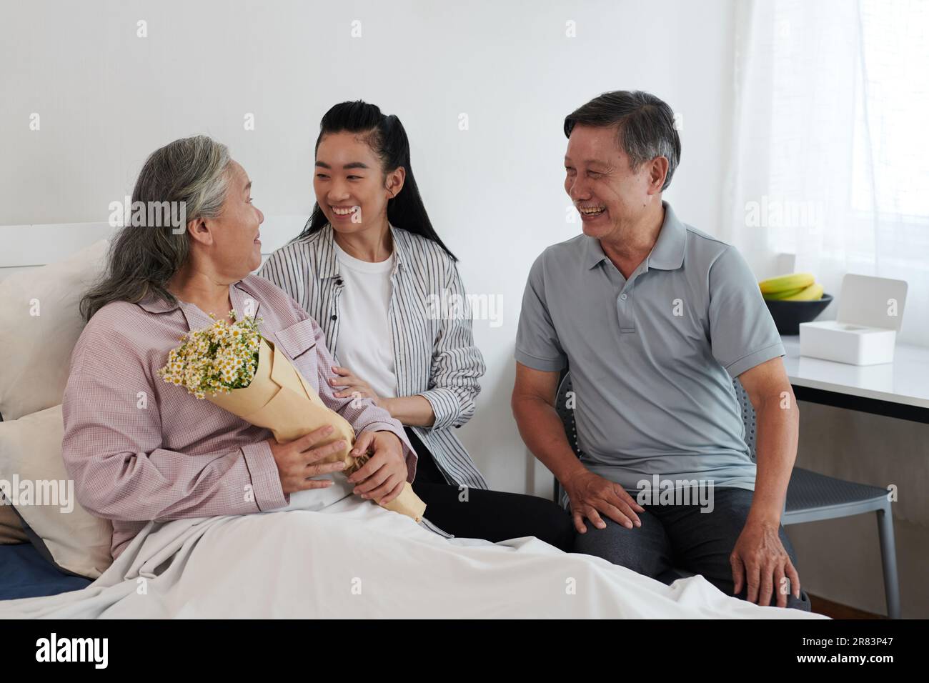 Husband and daughter bringing flowers to hispital ward of sick woman ...