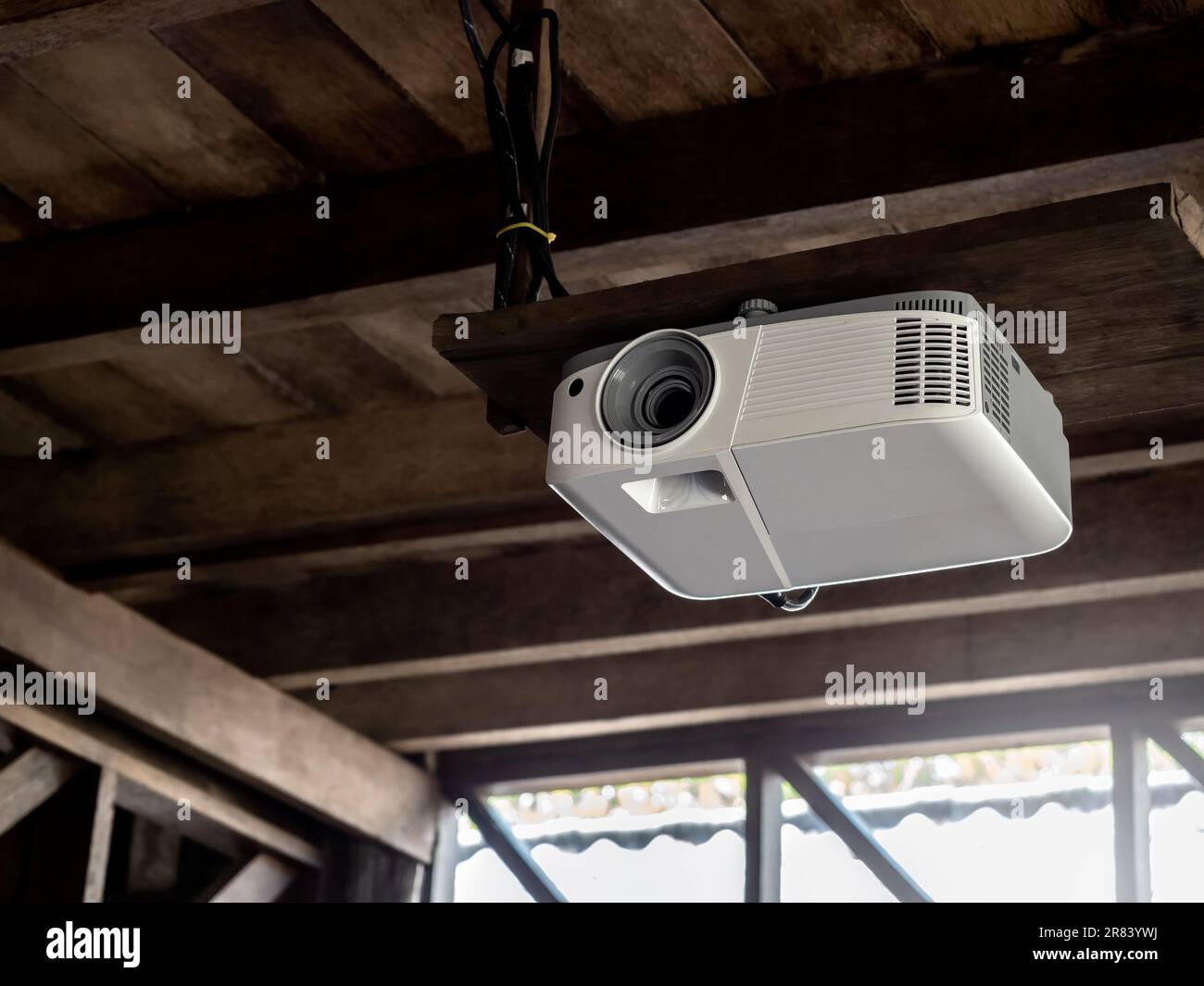 A white projector hangs on the brown wood ceiling of an old wooden ...