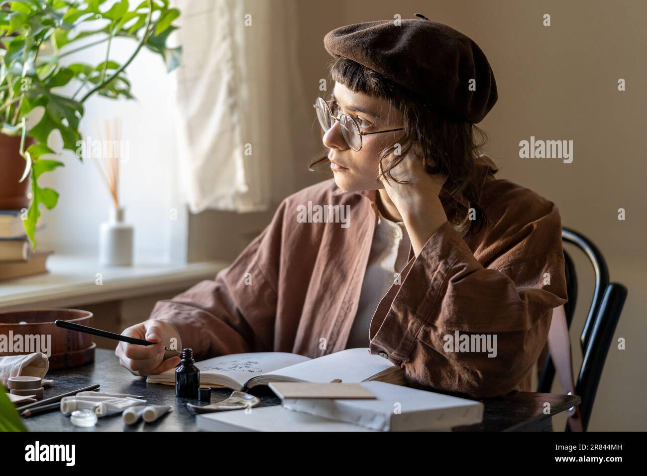 Pensive thoughtful female artist looking out window procrastinating ...