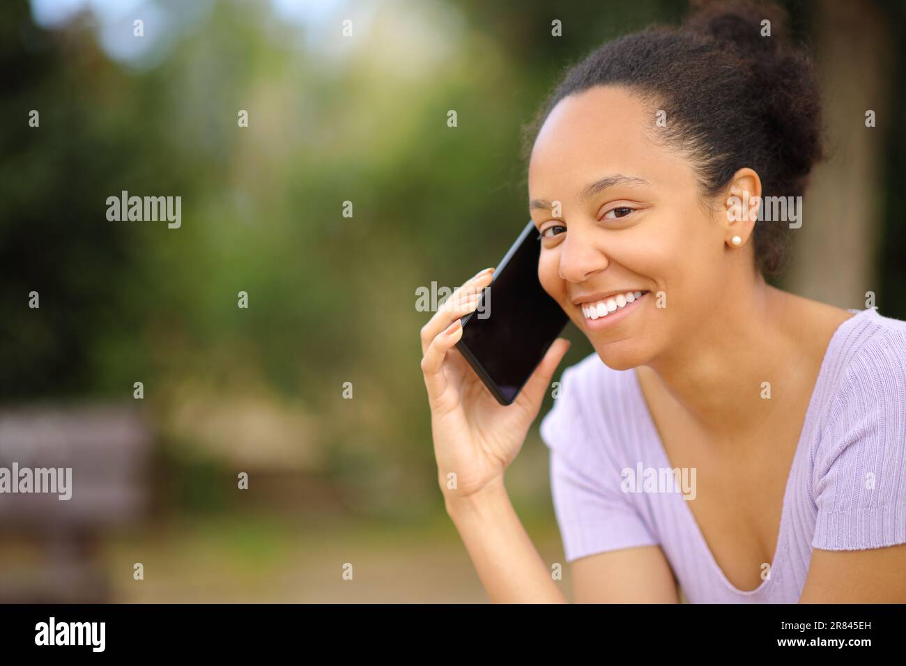 Happy black woman calling on phone looking at you in a park Stock Photo ...