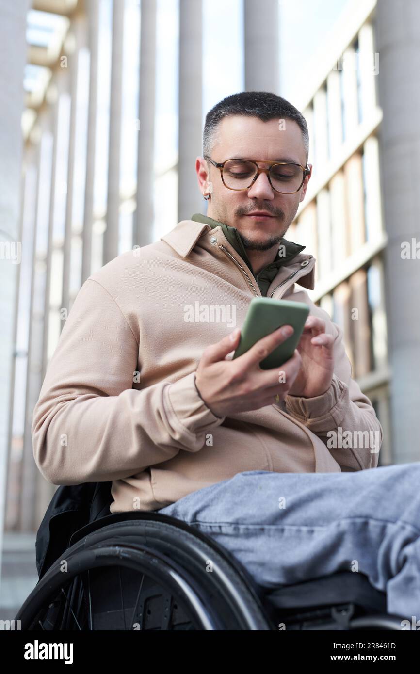 Vertical image of young man with disability typing message on his ...