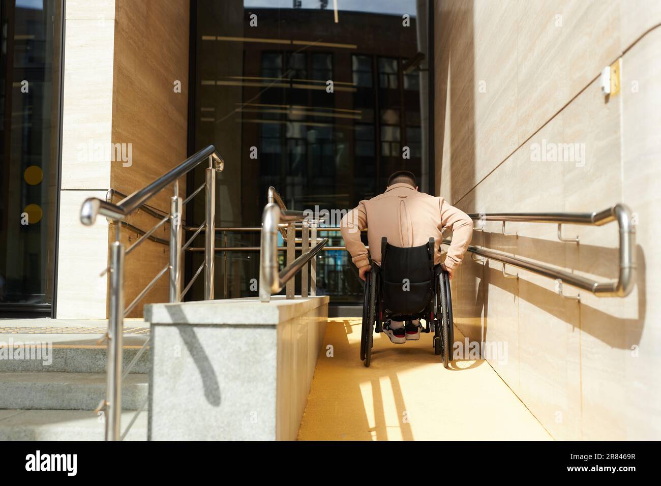 Rear view of young man with disability sitting in wheelchair and using ...