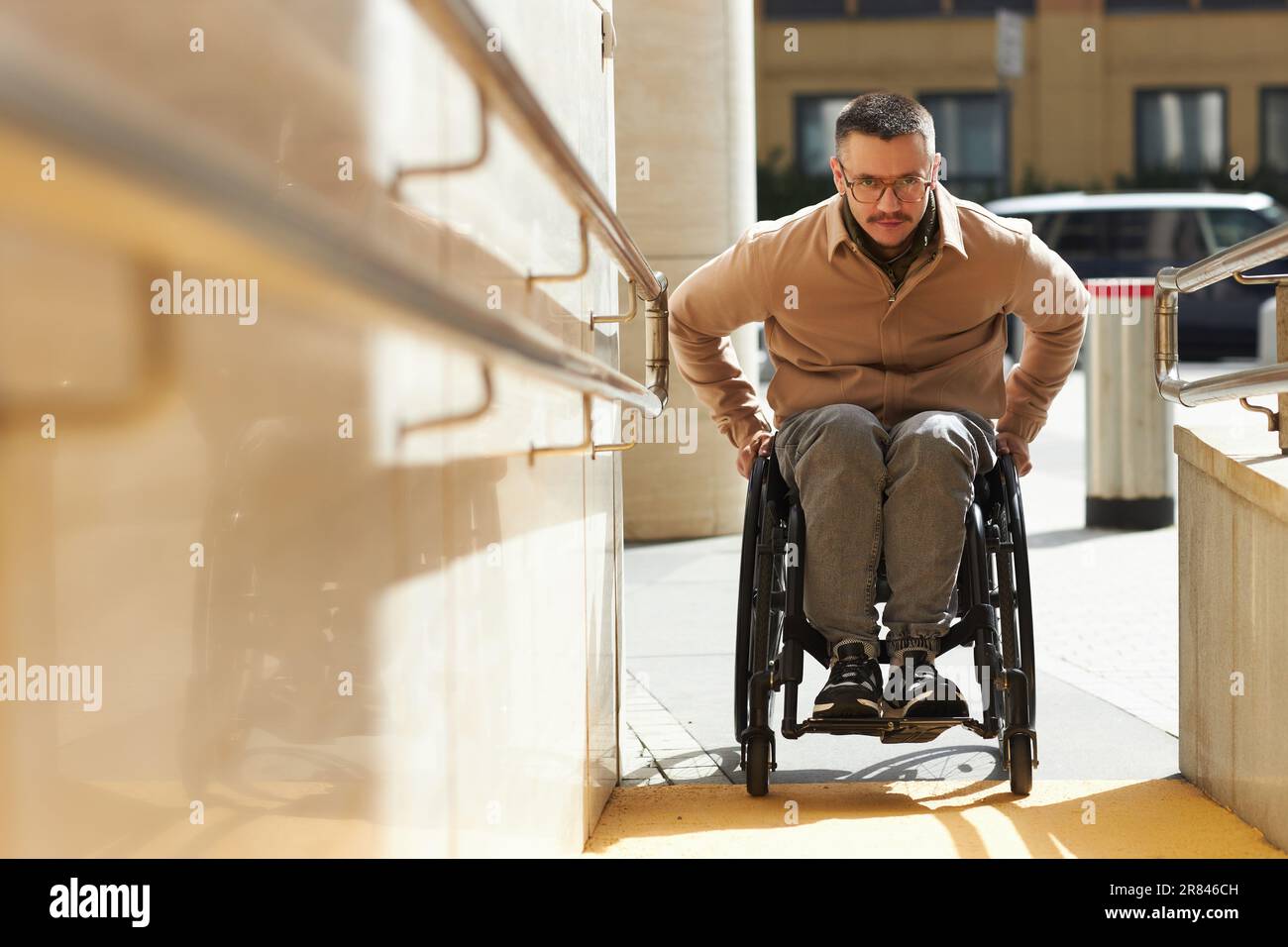 Young man in wheelchair moving up the ramp of building Stock Photo - Alamy