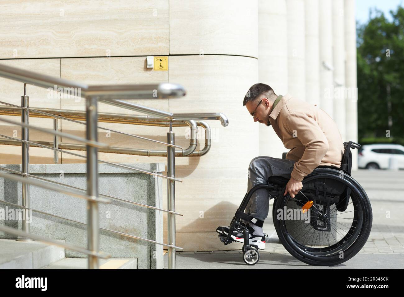 Side view of young man sitting in wheelchair using ramp to move up of ...