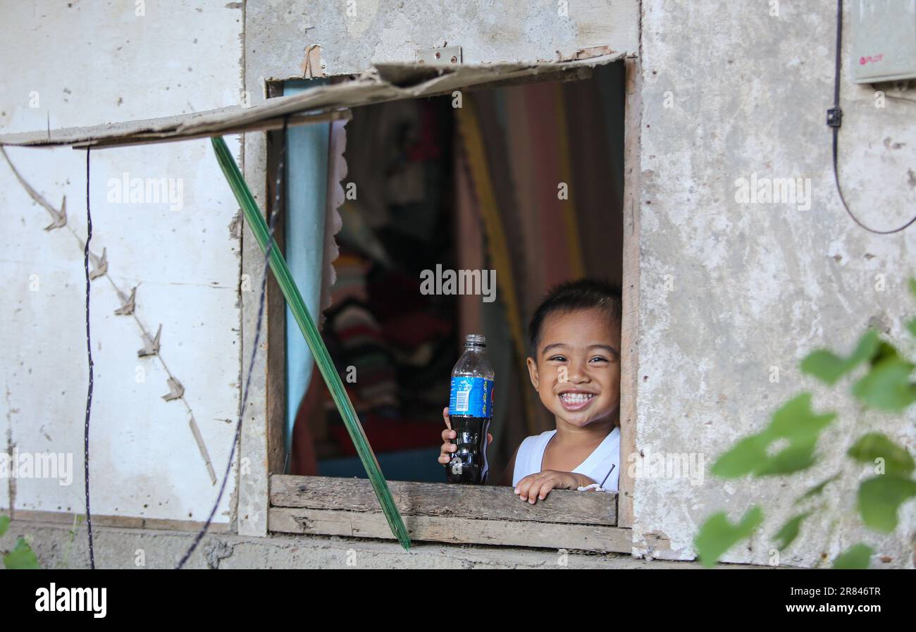 Young Filipino boy smiling through a top hung outward "window" in wood ...