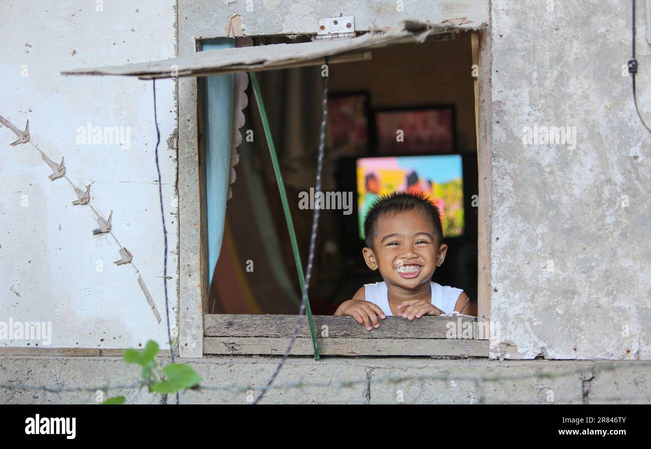 Young Filipino boy smiling through a top hung outward "window" in wood ...