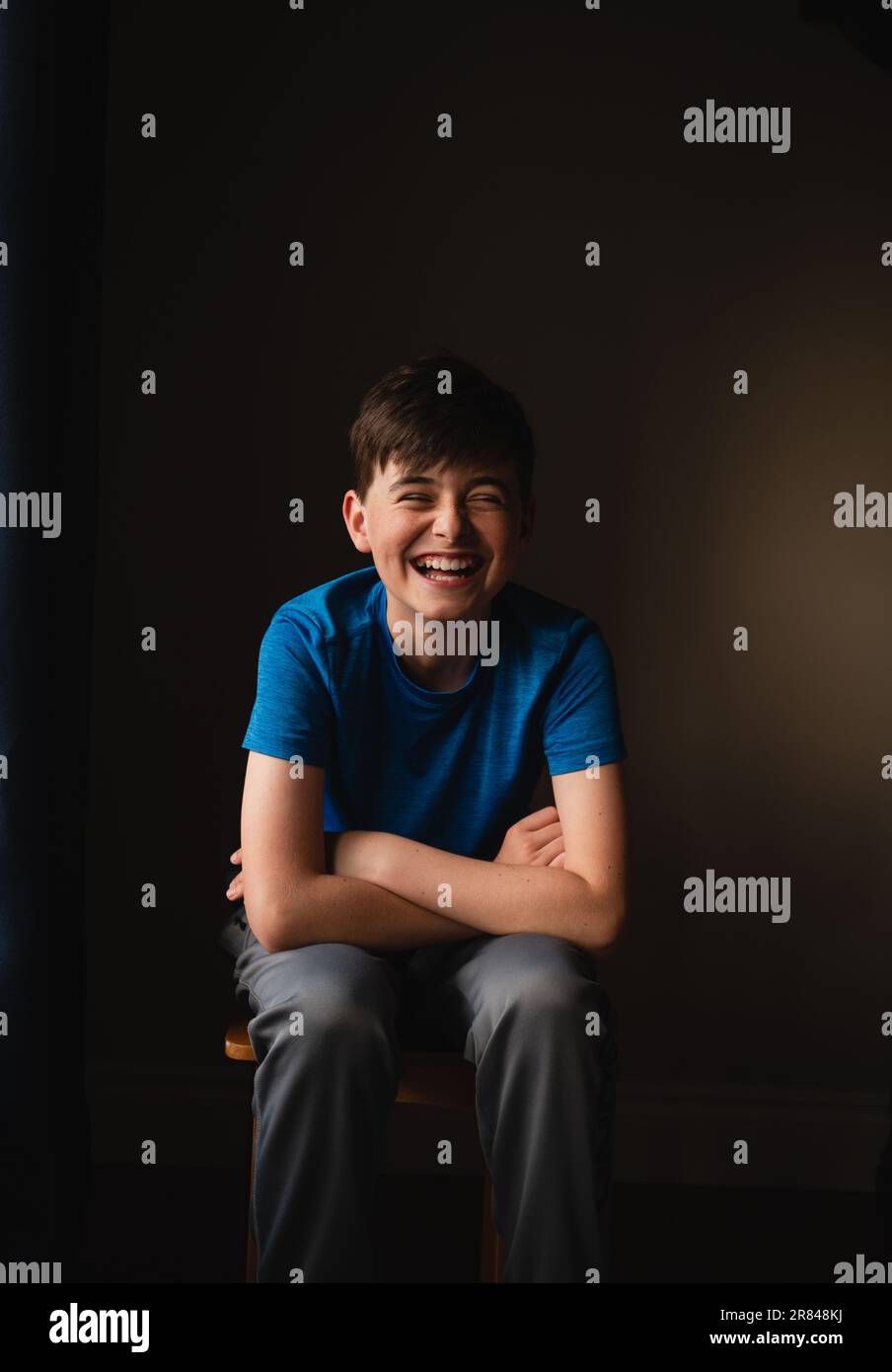 Portrait of laughing tween boy sitting on chair in dark room Stock ...