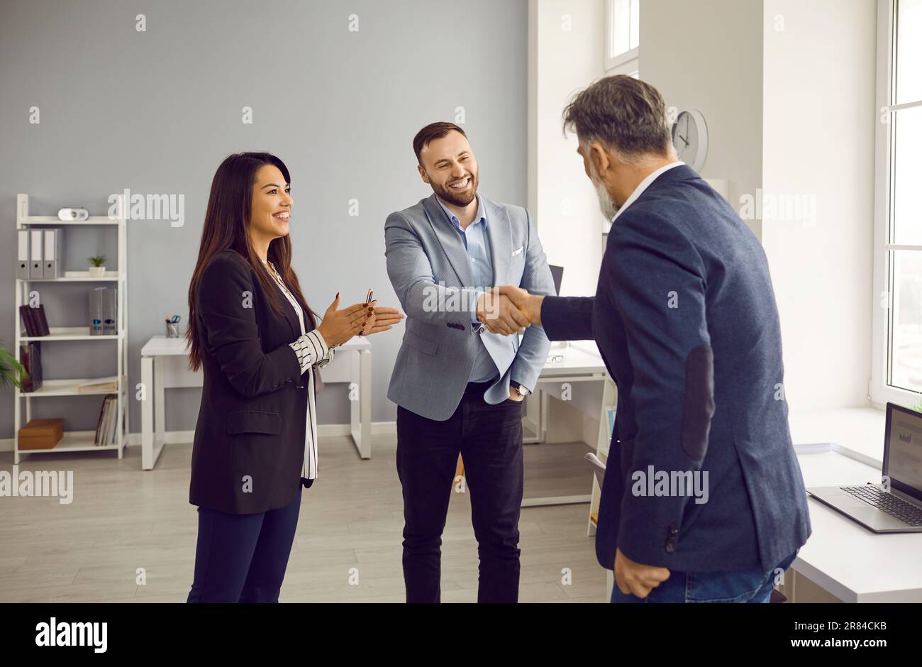 Business partners handshaking in office while female colleague ...