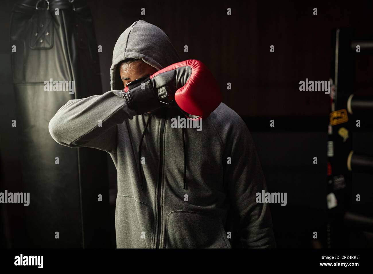 Young tired African American boxer in grey hoodie hiding his face ...