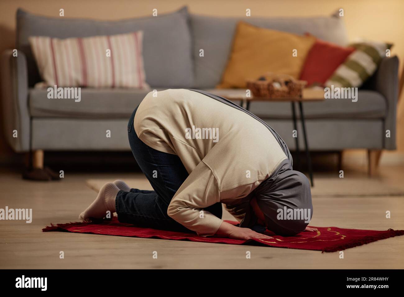 Young Muslim woman in grey hijab and casualwear bending forwards while ...