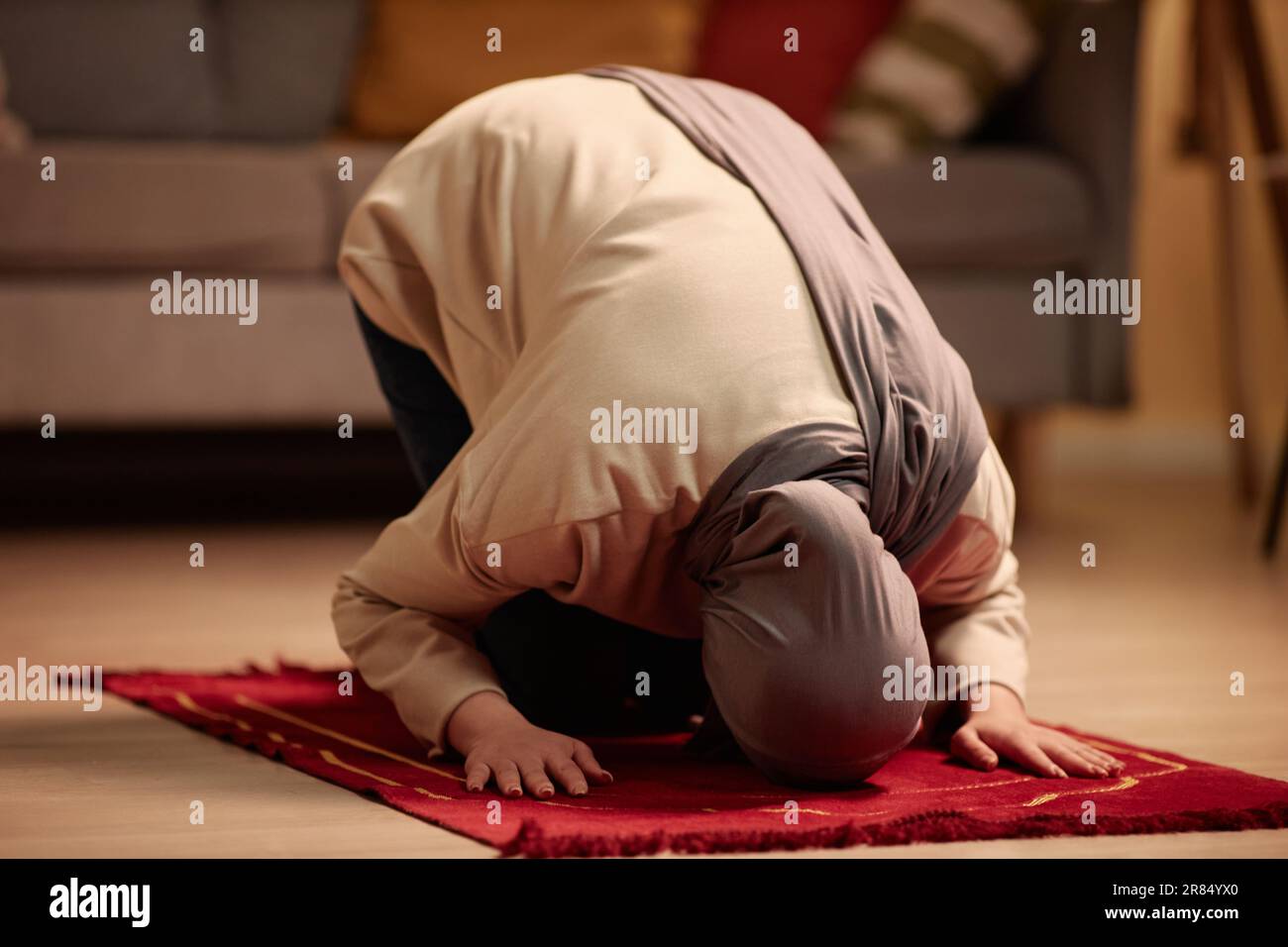 Back of young Muslim woman in hijab and beige pullover bending forwards ...