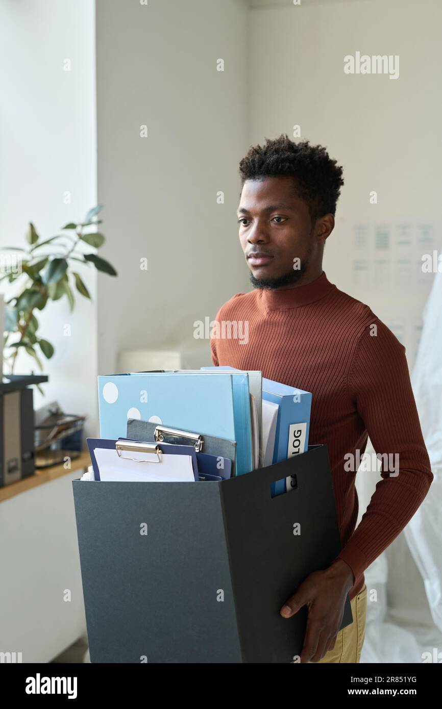 Vertical image of African American businessman carrying box with stuffs ...