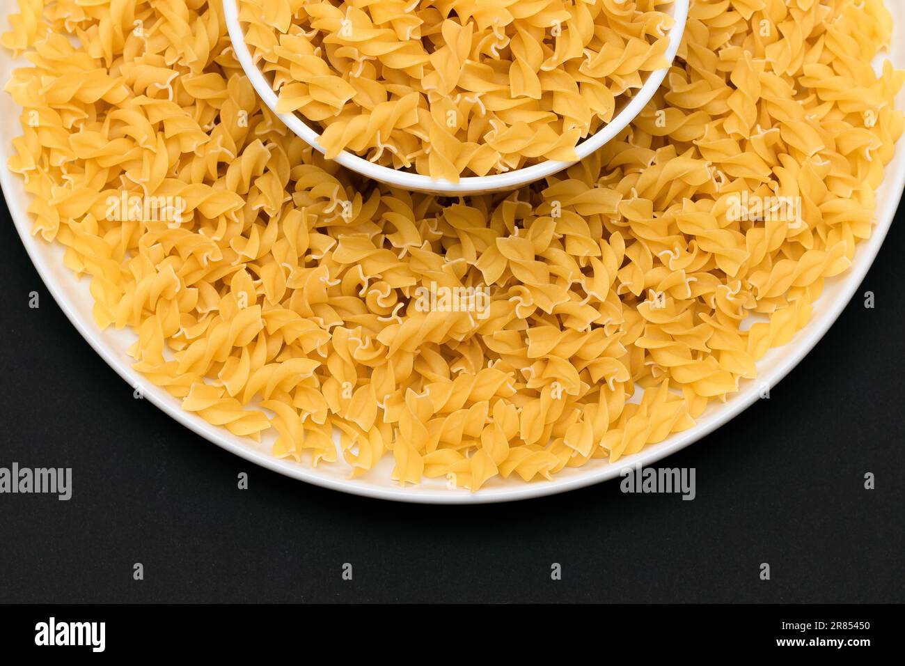 Uncooked Fusilli Pasta Lying on White Plate on Black Background. Raw ...