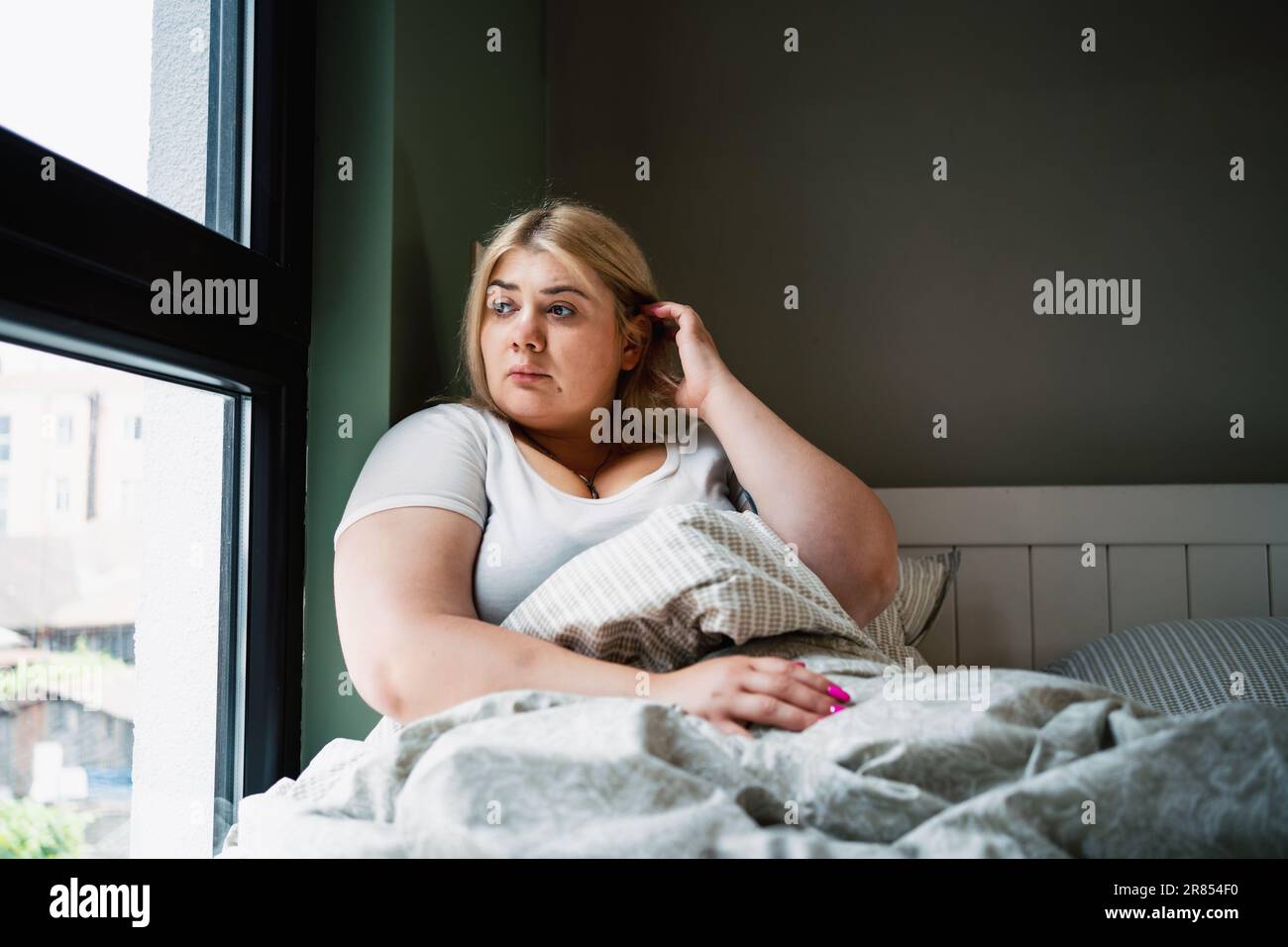 Unhappy sad depressed lonely plus size overweight woman looks at window ...