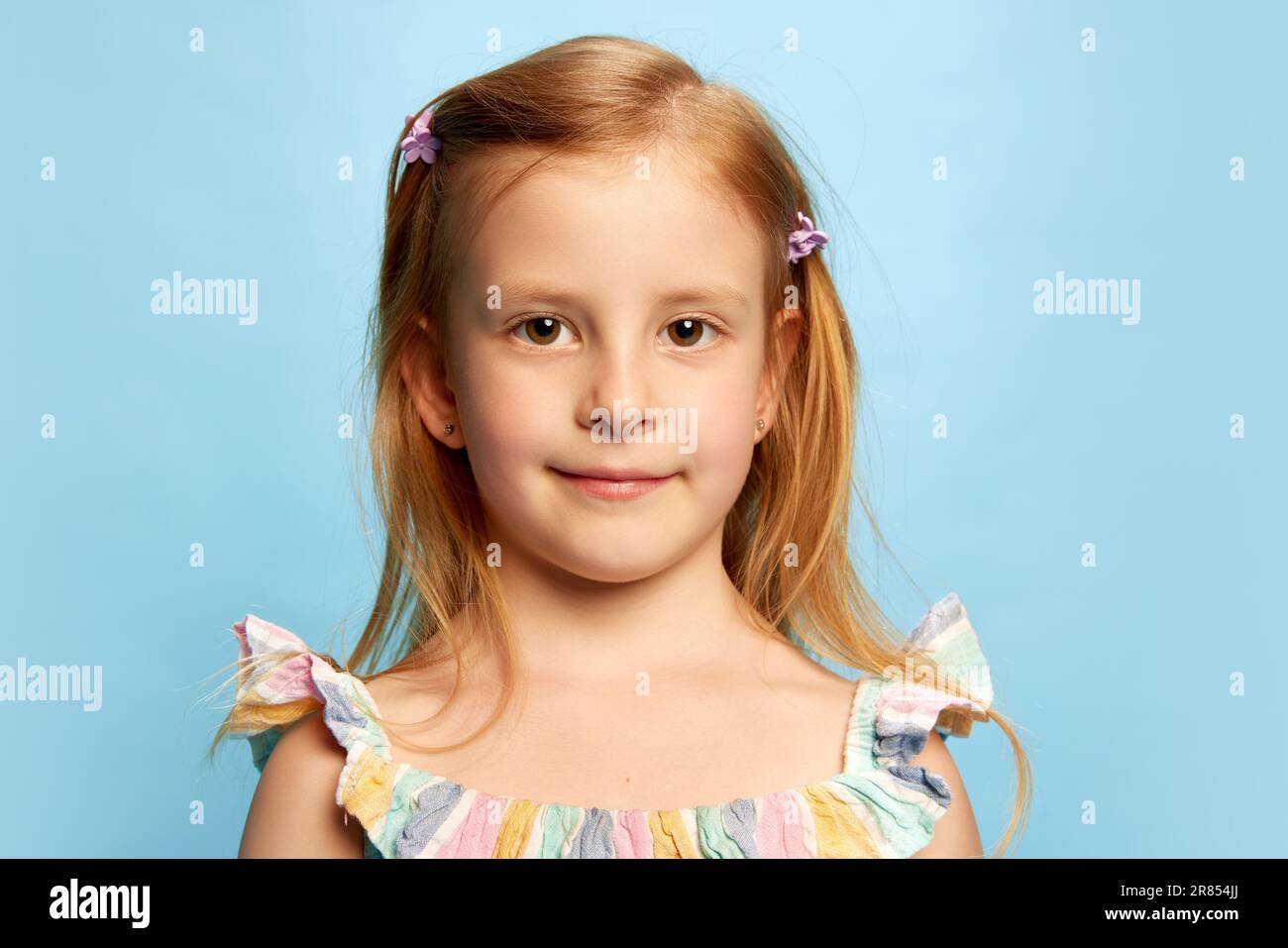 Close-up portrait of pretty little girl, redhead child with cute hairstyle looking at camera ...