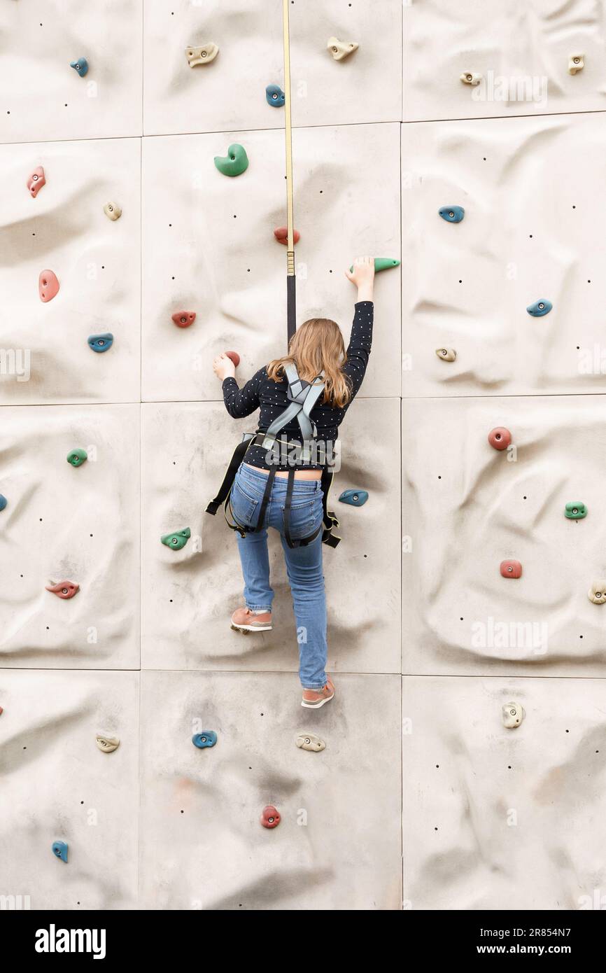 Teenage teen girl grabbing artificial high climbing wall with split ...