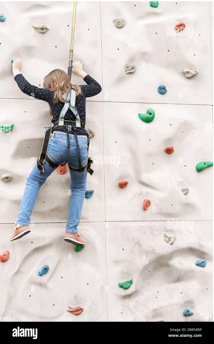 Teenage teen girl grabbing artificial high climbing wall with split ...