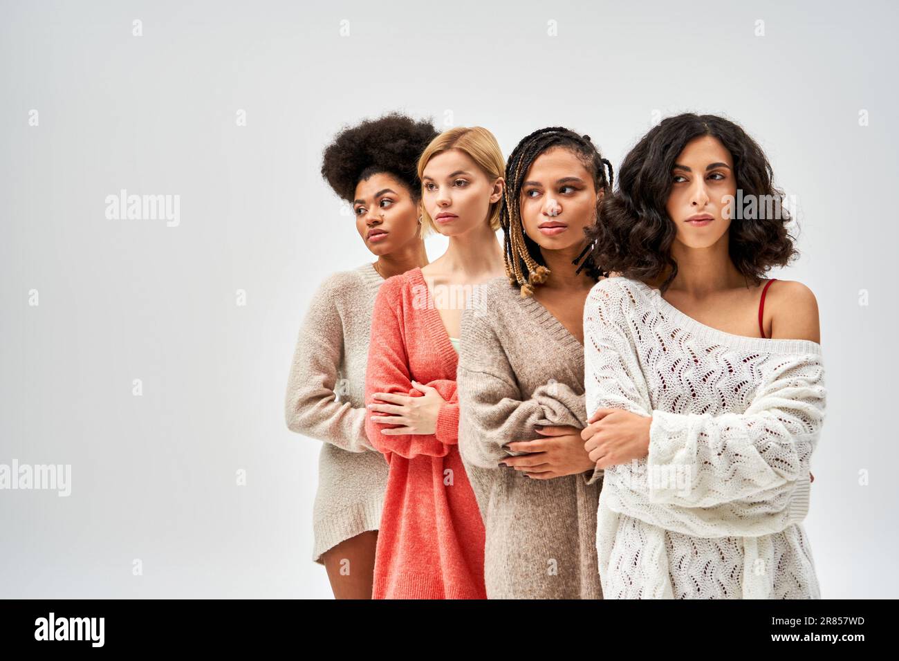 Stylish multiethnic women in trendy knitted jumpers crossing arms and ...