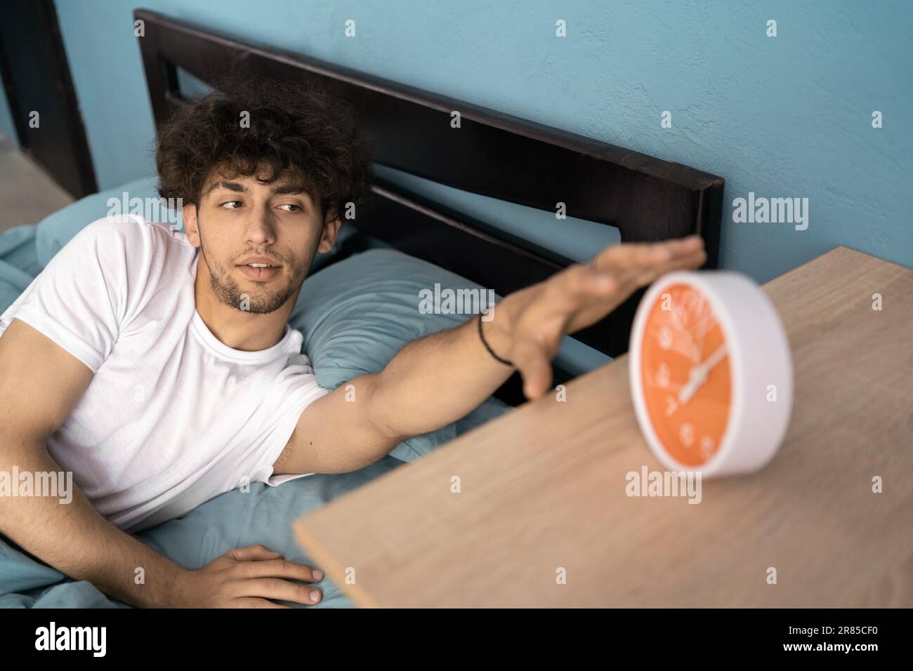 Happy young man 20s lies in bed under blanket duvet on pillow turn off ...