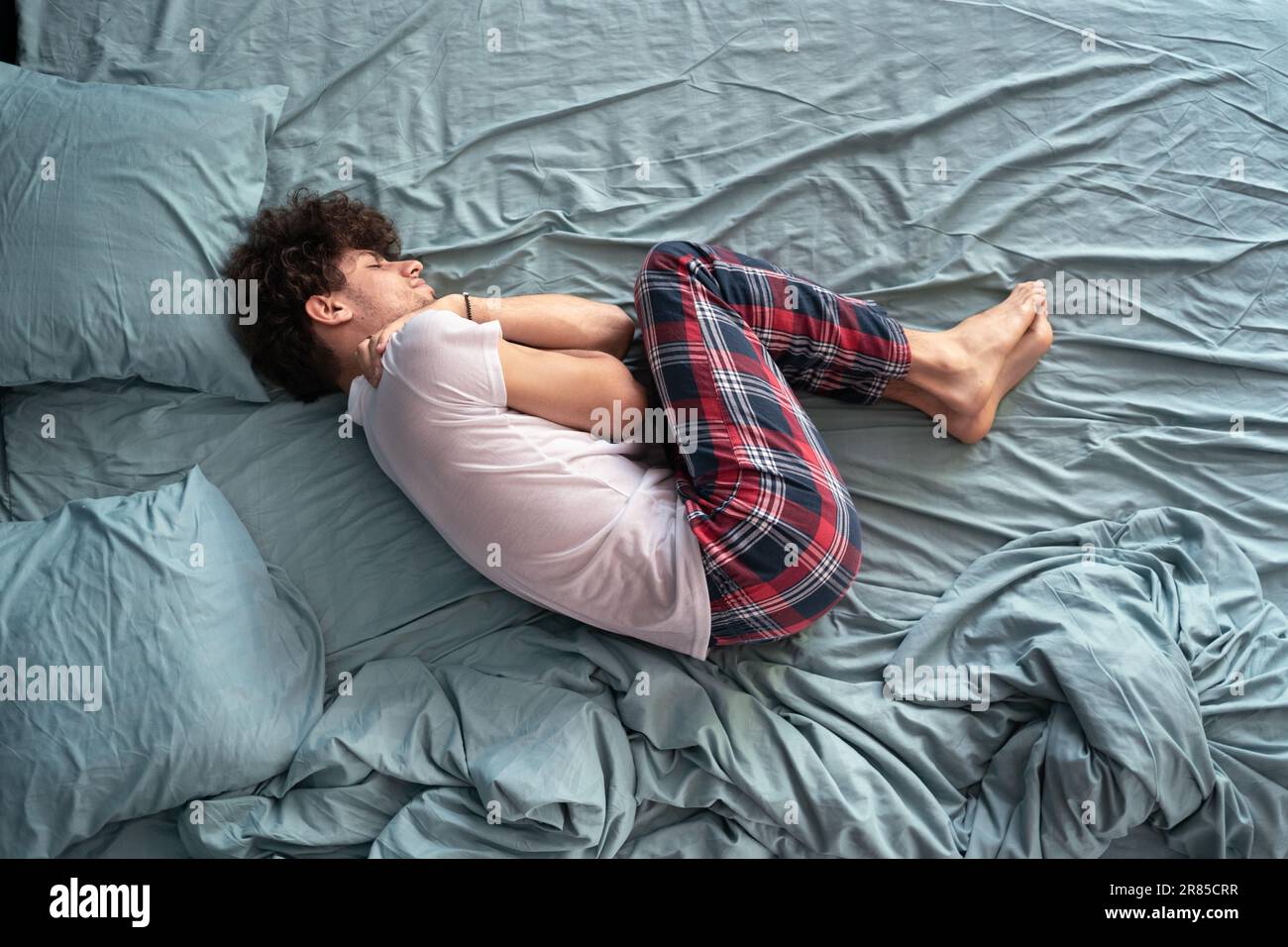 Top view stressed unhappy young man lying in fetal position on bed alone, upset guy suffering ...