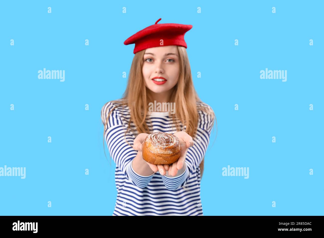 Young woman in beret with tasty bun on blue background Stock Photo - Alamy