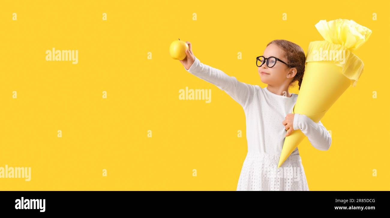 Cute little girl with school cone and apple on yellow background with ...