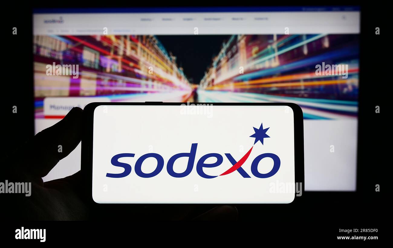 Person holding smartphone with logo of French facility management company Sodexo S.A. on screen ...