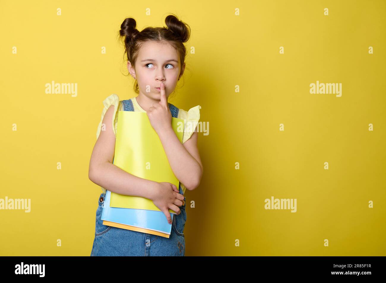 Smart primary school student girl with textbooks, puts index finger on ...