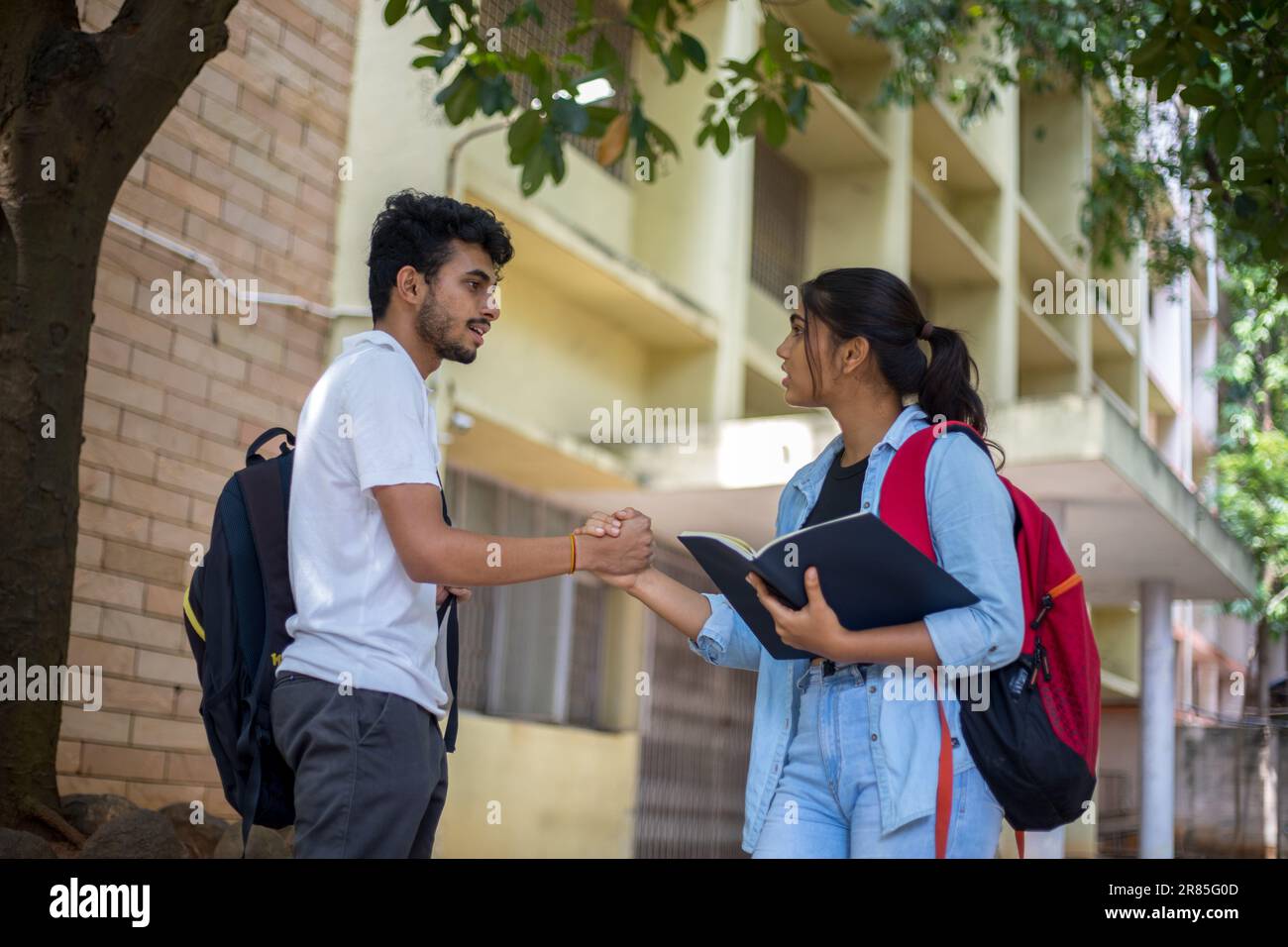 Happy young students giving a handshake to their classmates in campus ...