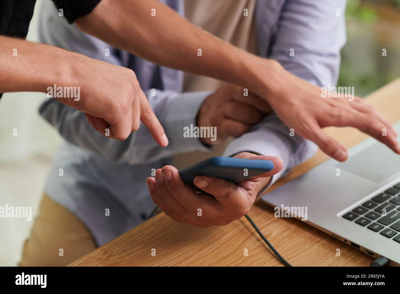 Hands of young man showing father how to transfer files from smartphone ...
