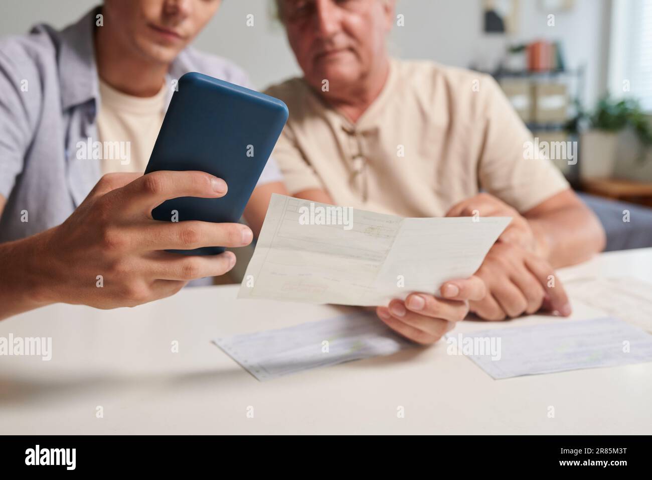 Young man helping grandfather to pay utility bills via mobile ...