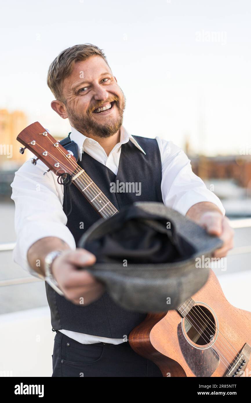 A smiling street musician looking at camera and carrying his guitar ...