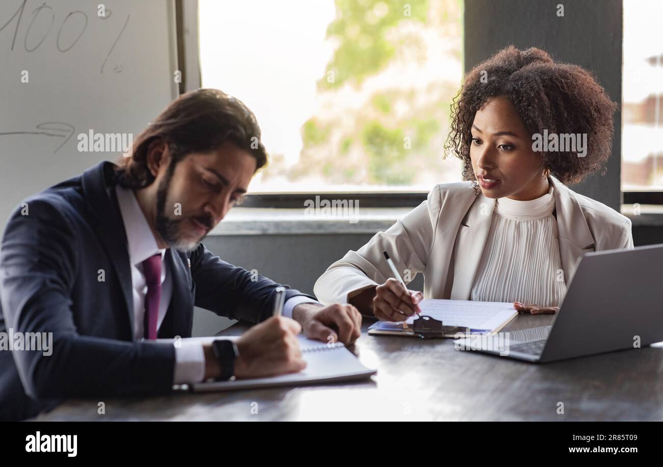 Multiethnic management team taking notes during meeting at office Stock ...
