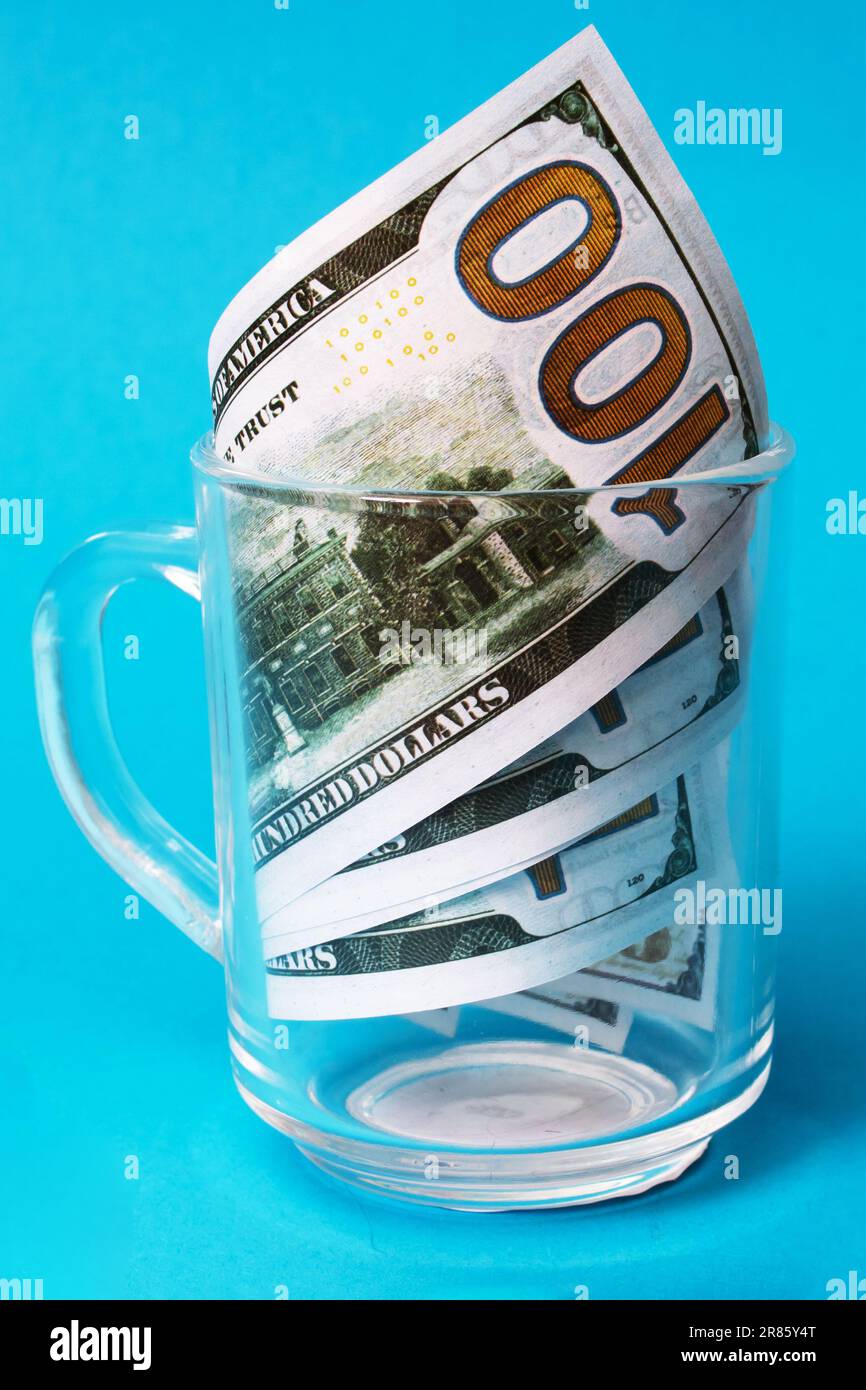 Dollar bills in a transparent mug on blue background Stock Photo - Alamy