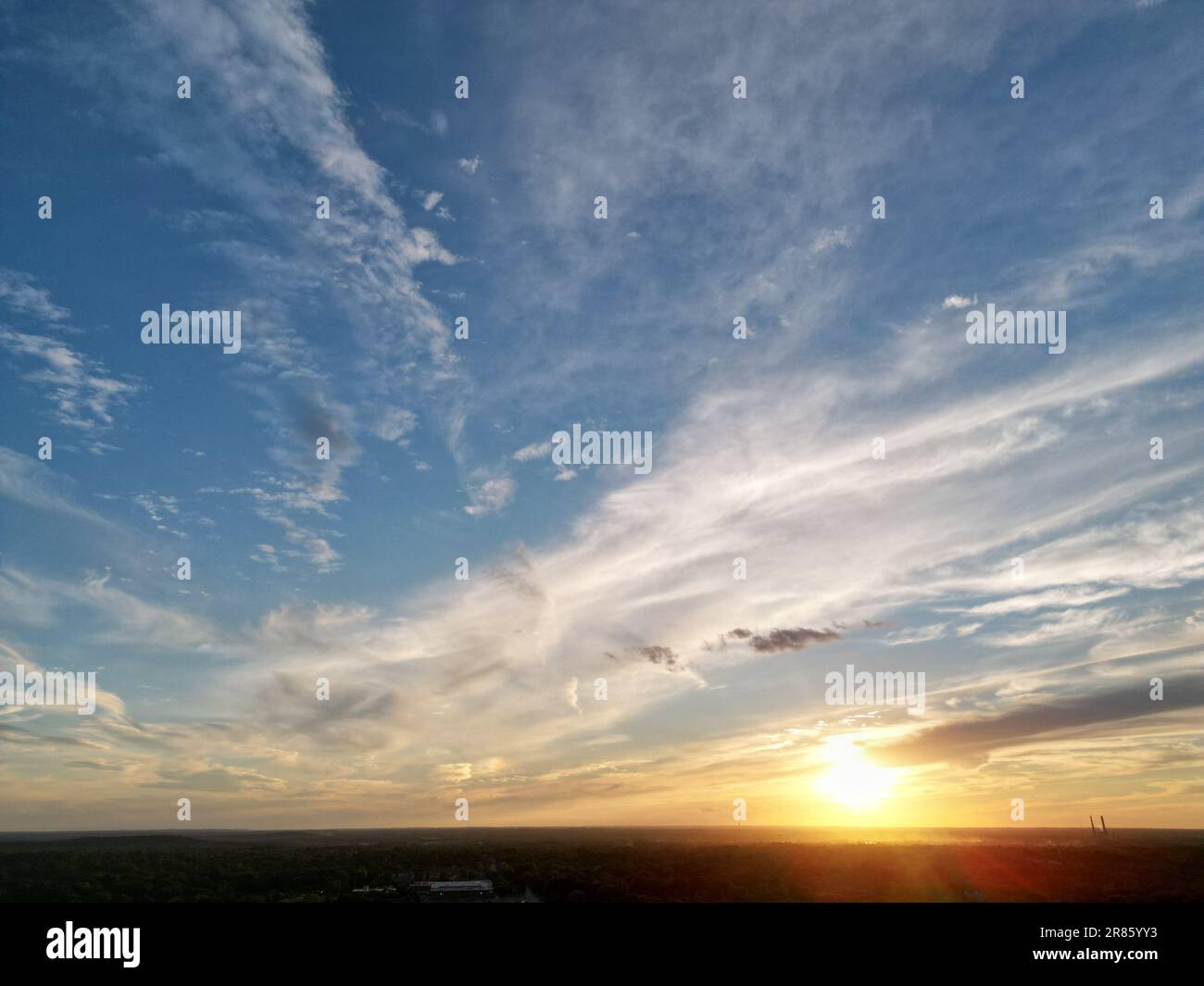 A picturesque sunset radiates across the sky with fluffy white clouds ...